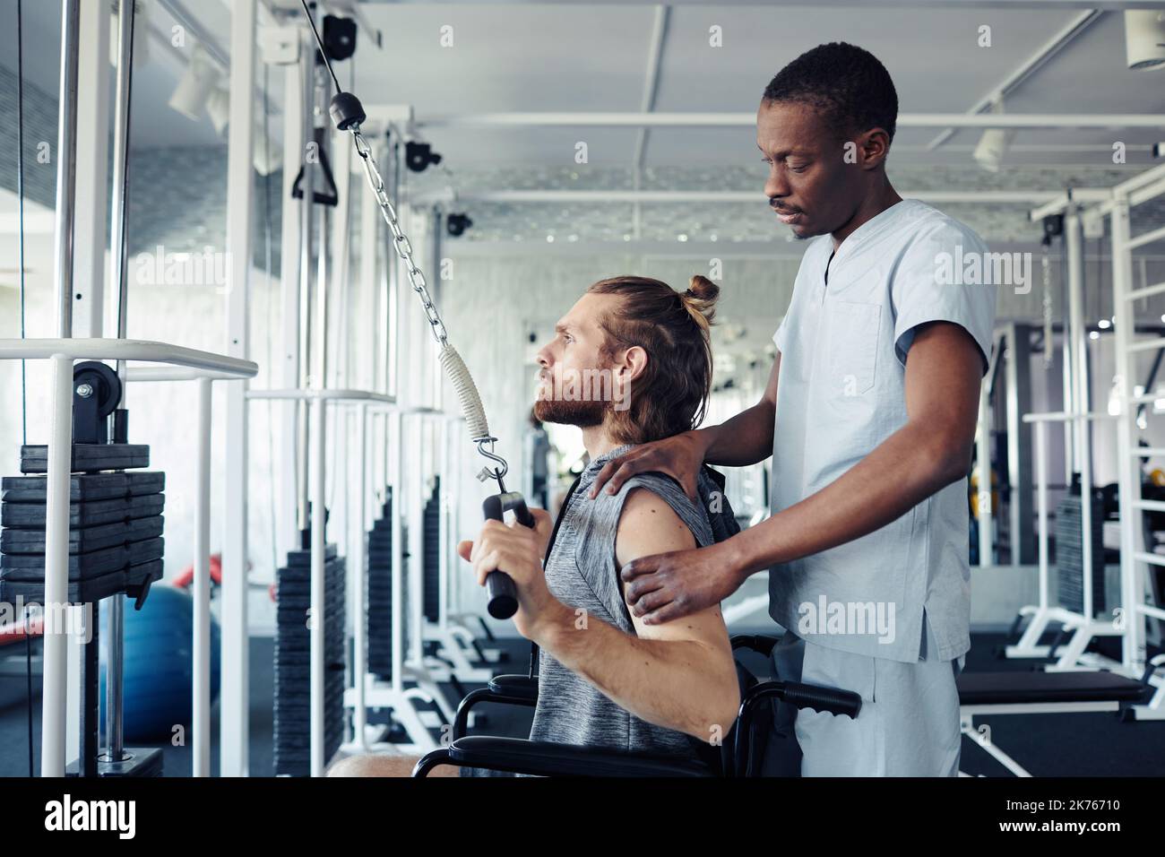 African doctor training patient with disability on exercise equipment ...