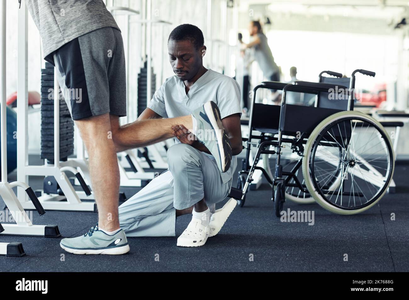 African young therapist helping patient to do physical exercise on ...