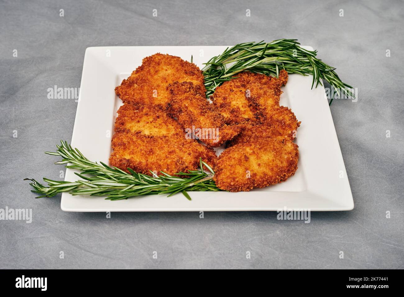 Organic breaded chicken cutlet served on a plate with rosemary garnish ...