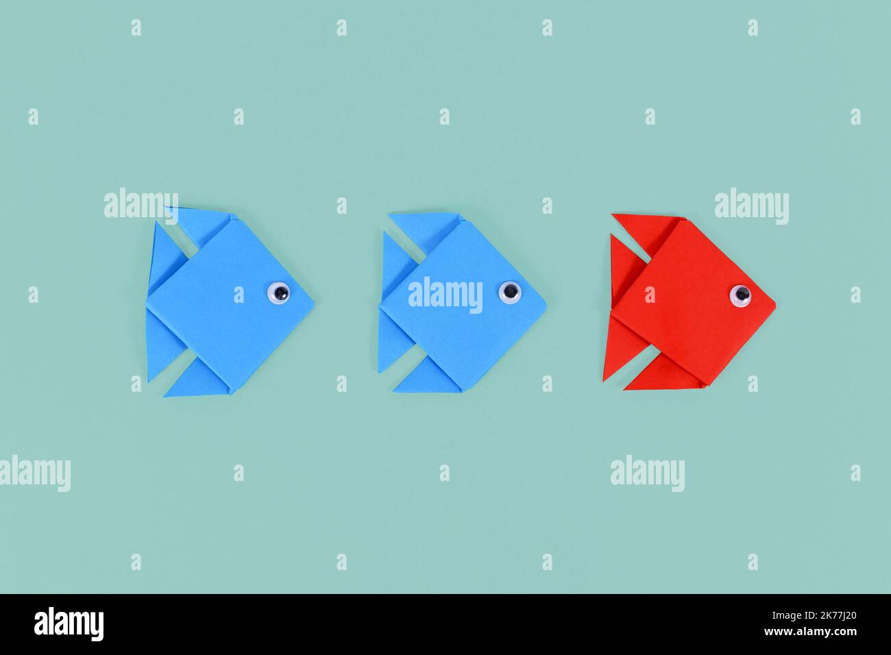 Red origami paper fish swimming in front of blue fish. Concept for ...