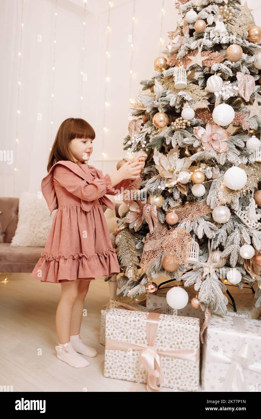 Little girl in festive soft pink dress is decorating Christmas tree ...