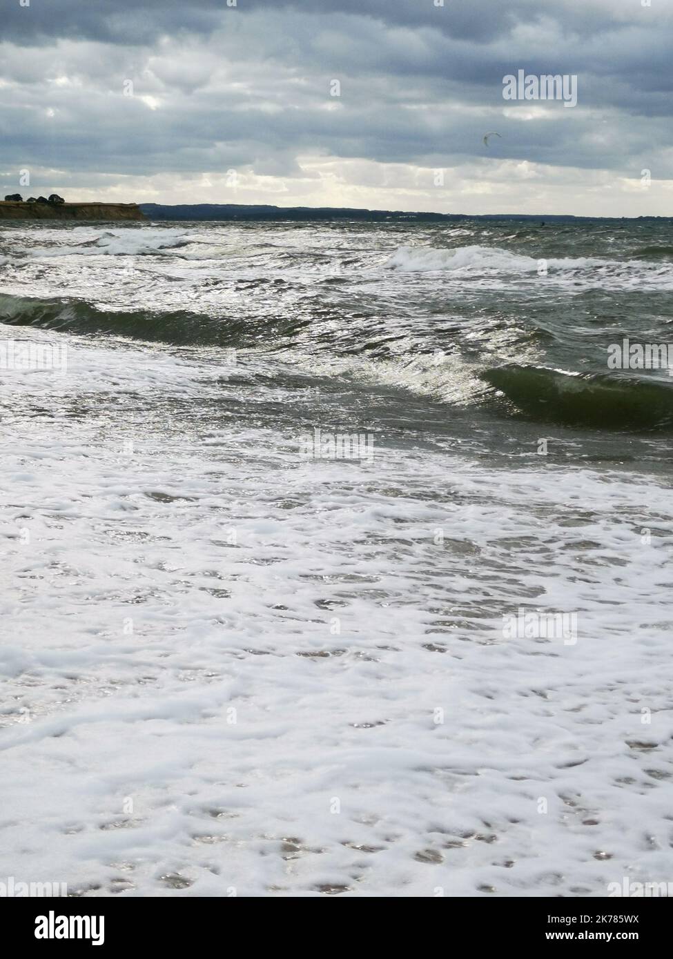 A vertical closeup of a stormy sea making foam on the beach, gloomy ...