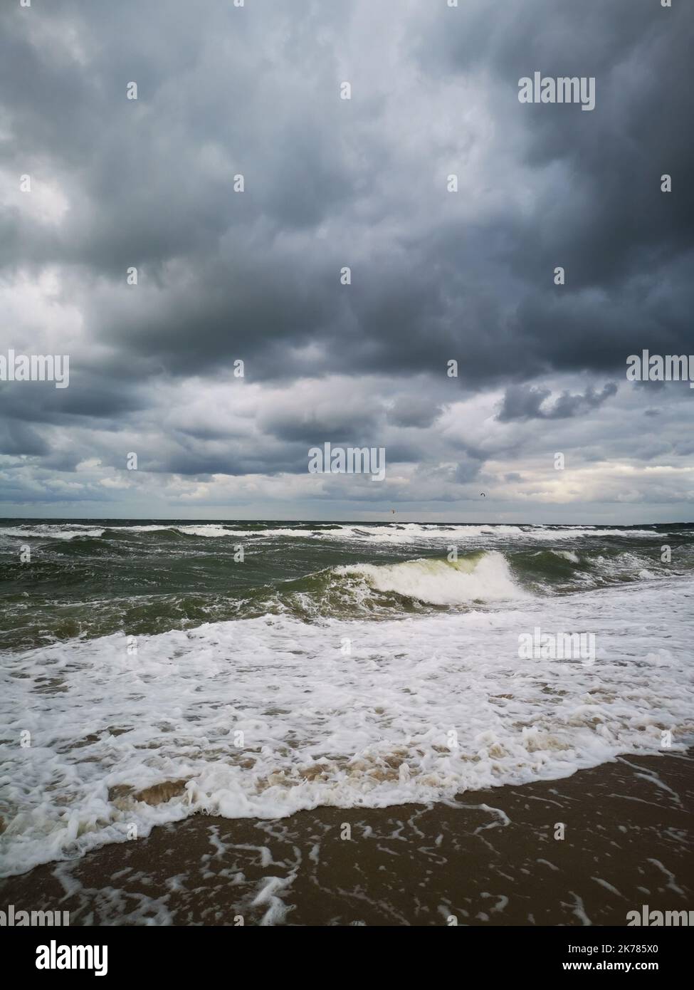 A vertical closeup of a stormy sea making foam on the beach, gloomy ...