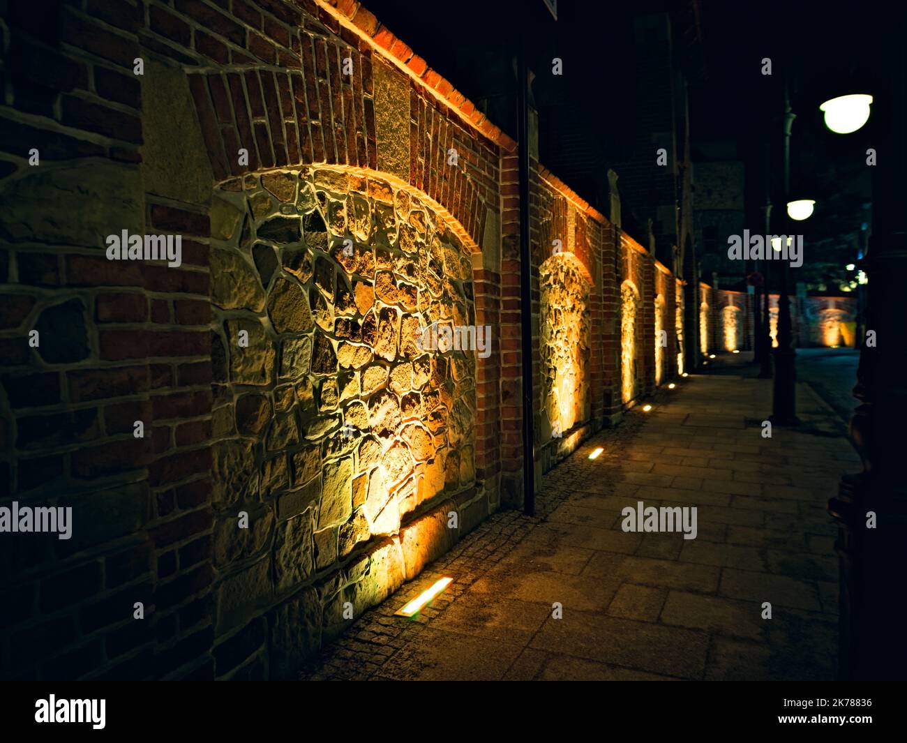 Illuminated stone wall at night with an alley with street lamps and a ...