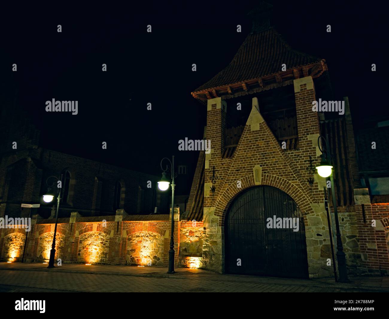 Illuminated stone wall at night with an alley with street lamps and a ...