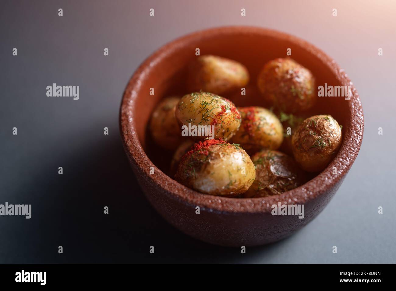 roasted potatoes with herbs and spice in clay bowl on black background ...