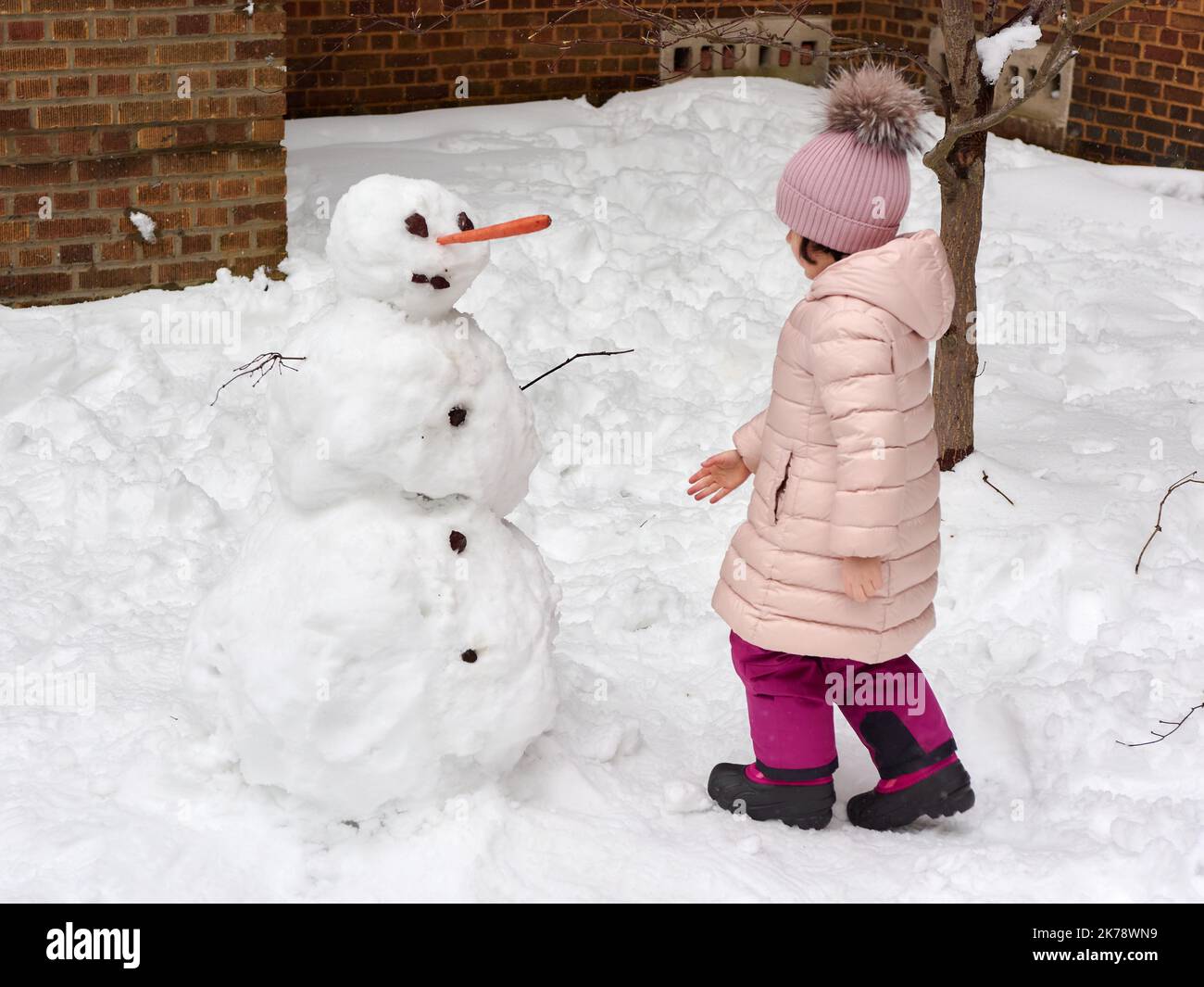 Little girl dressed in pink winter atire is putting the finishing ...