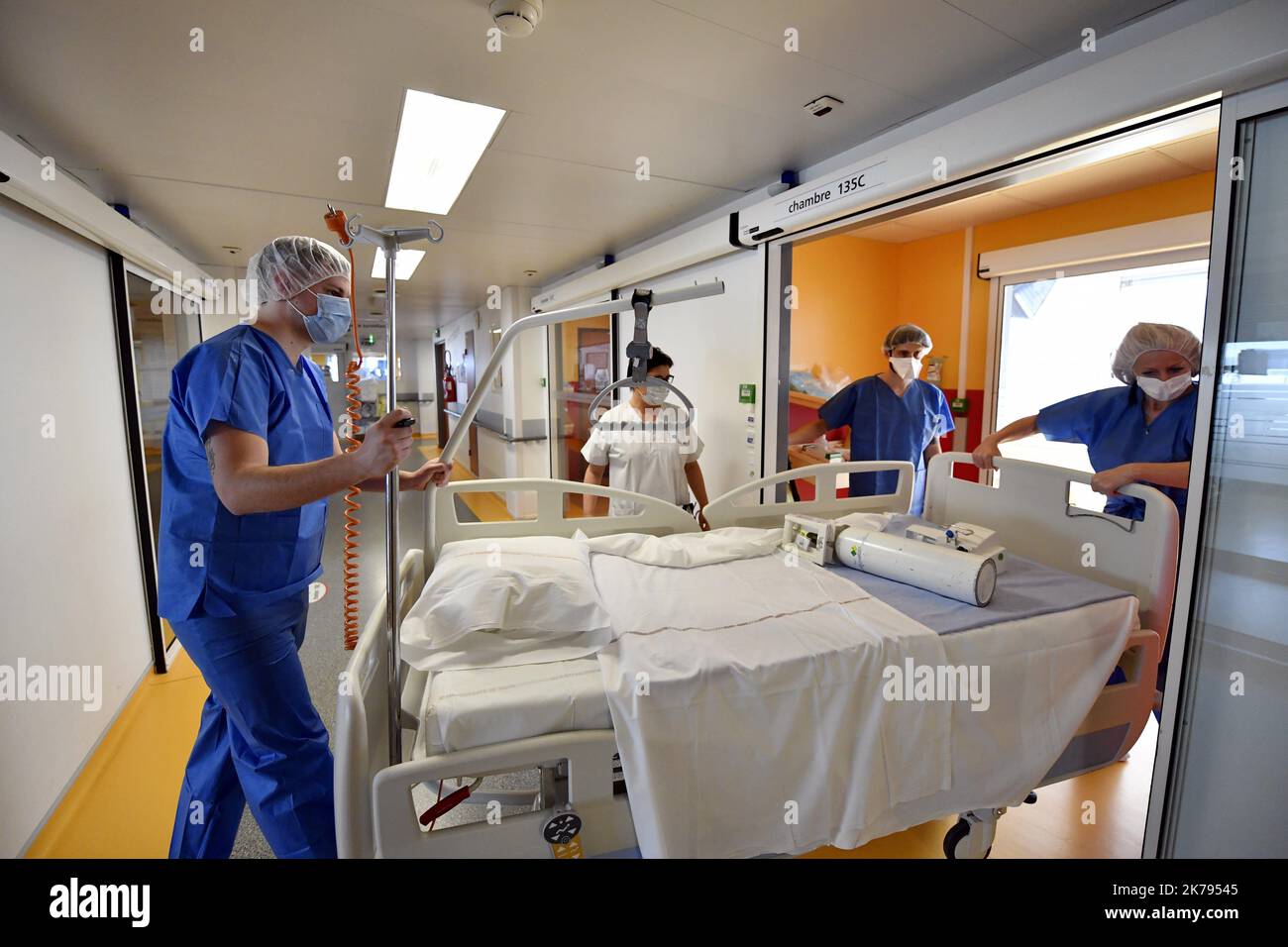 Hospital staff wear protective masks whilst moving a bed in a corridor ...