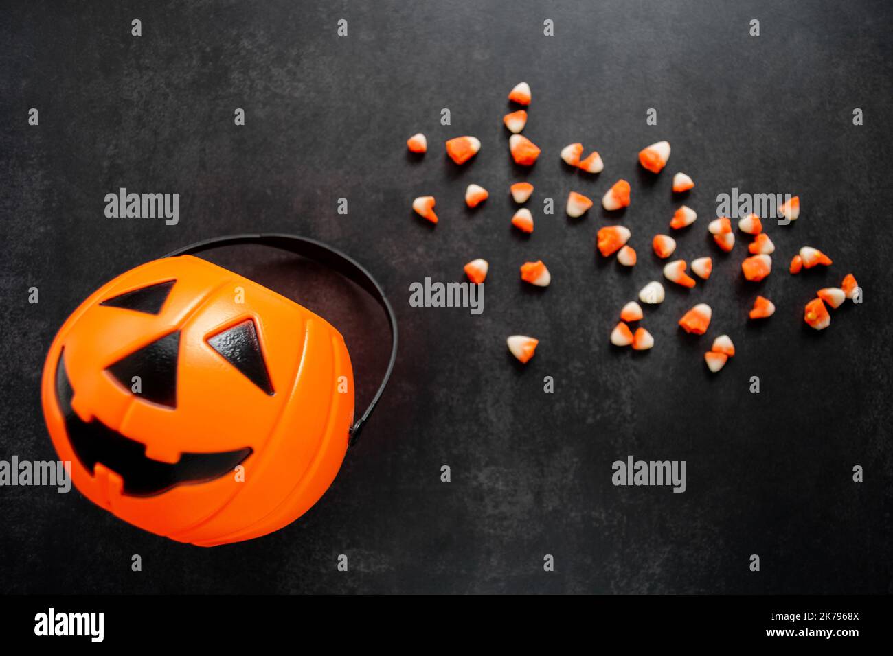 Plastic pumpkin basket with candy corn spilled out. Some of it are ...