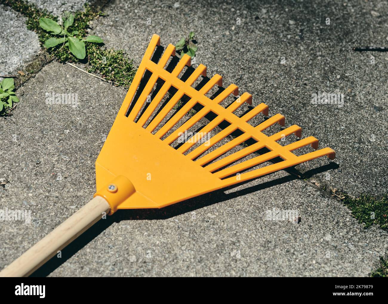 a flimsy plastic orange rake with a wooden handle is lying on the stone ...