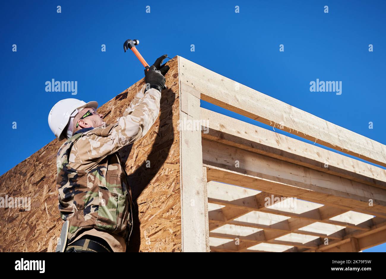Carpenter hammering nail into OSB panel on the wall of future cottage ...