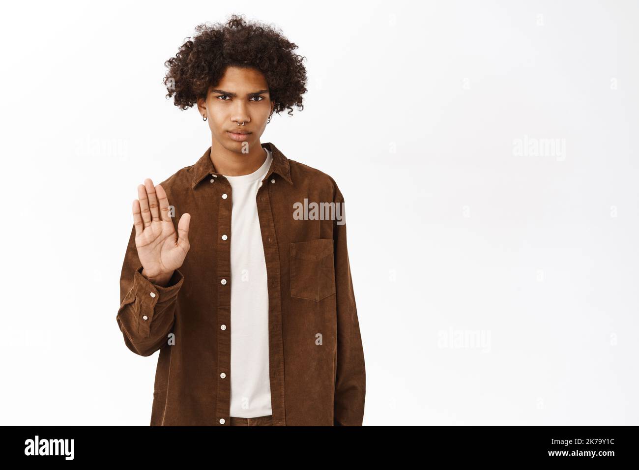 Serious young man shows stop hand gesture, extends arm, saying no, stay ...