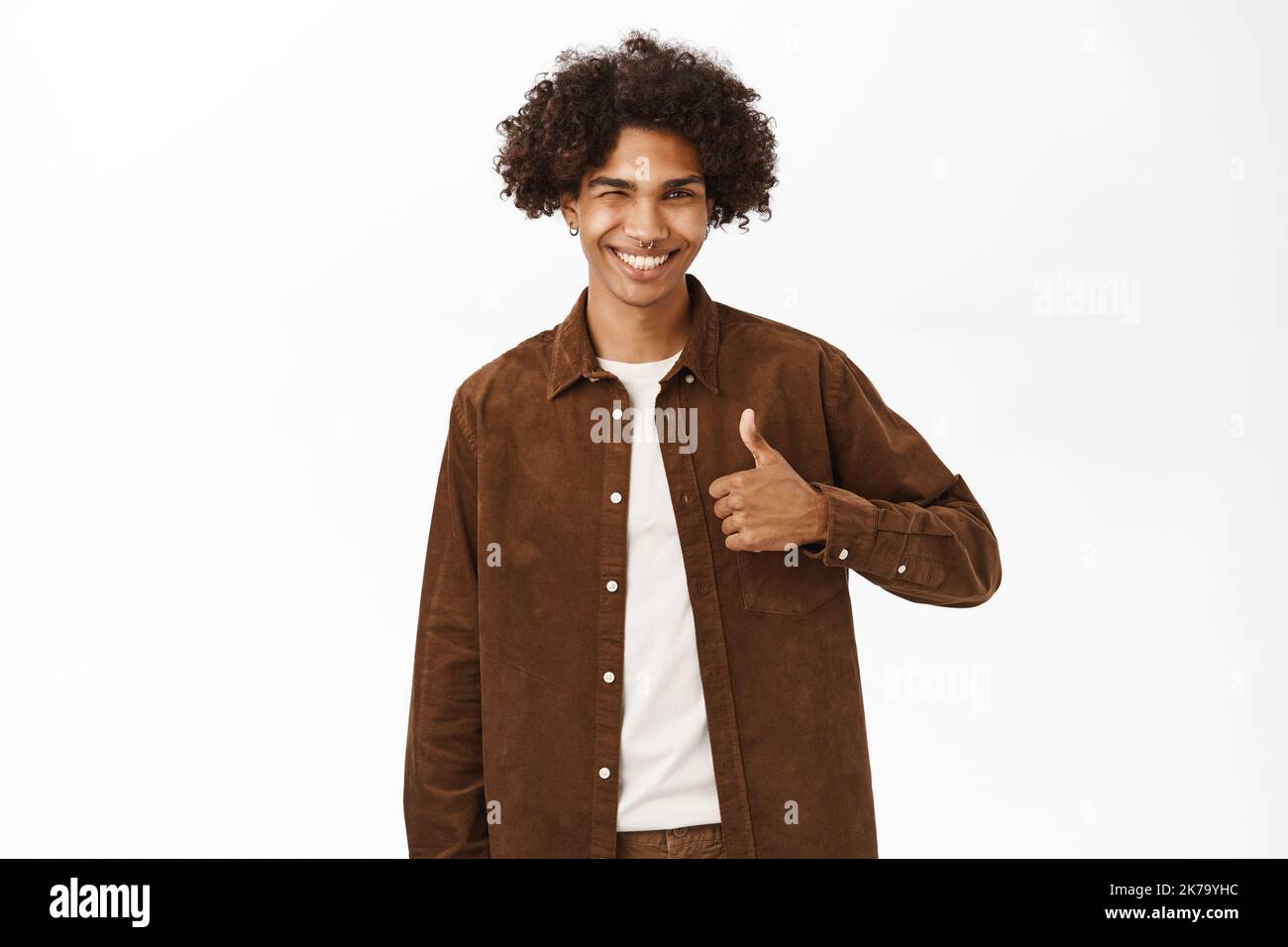 Handsome boy shows thumbs up and smiles pleased, stands over white ...