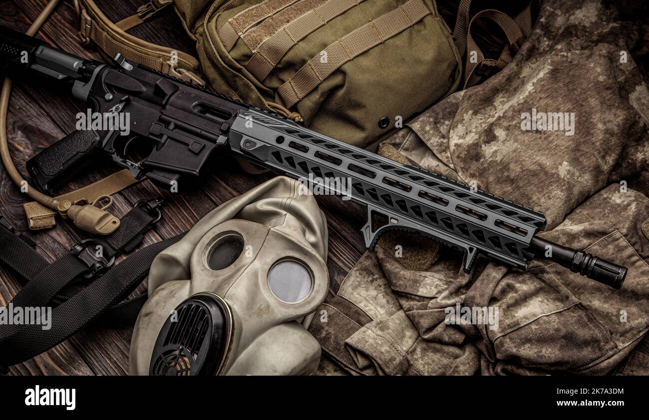 Modern automatic carbine, backpack and gas mask on a wooden table. A ...