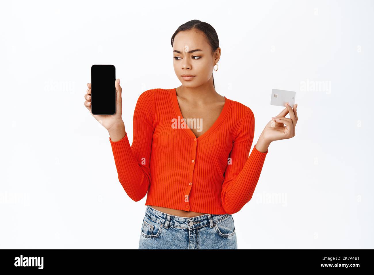 Disappointed woman showing credit card, looking upset at mobile phone ...