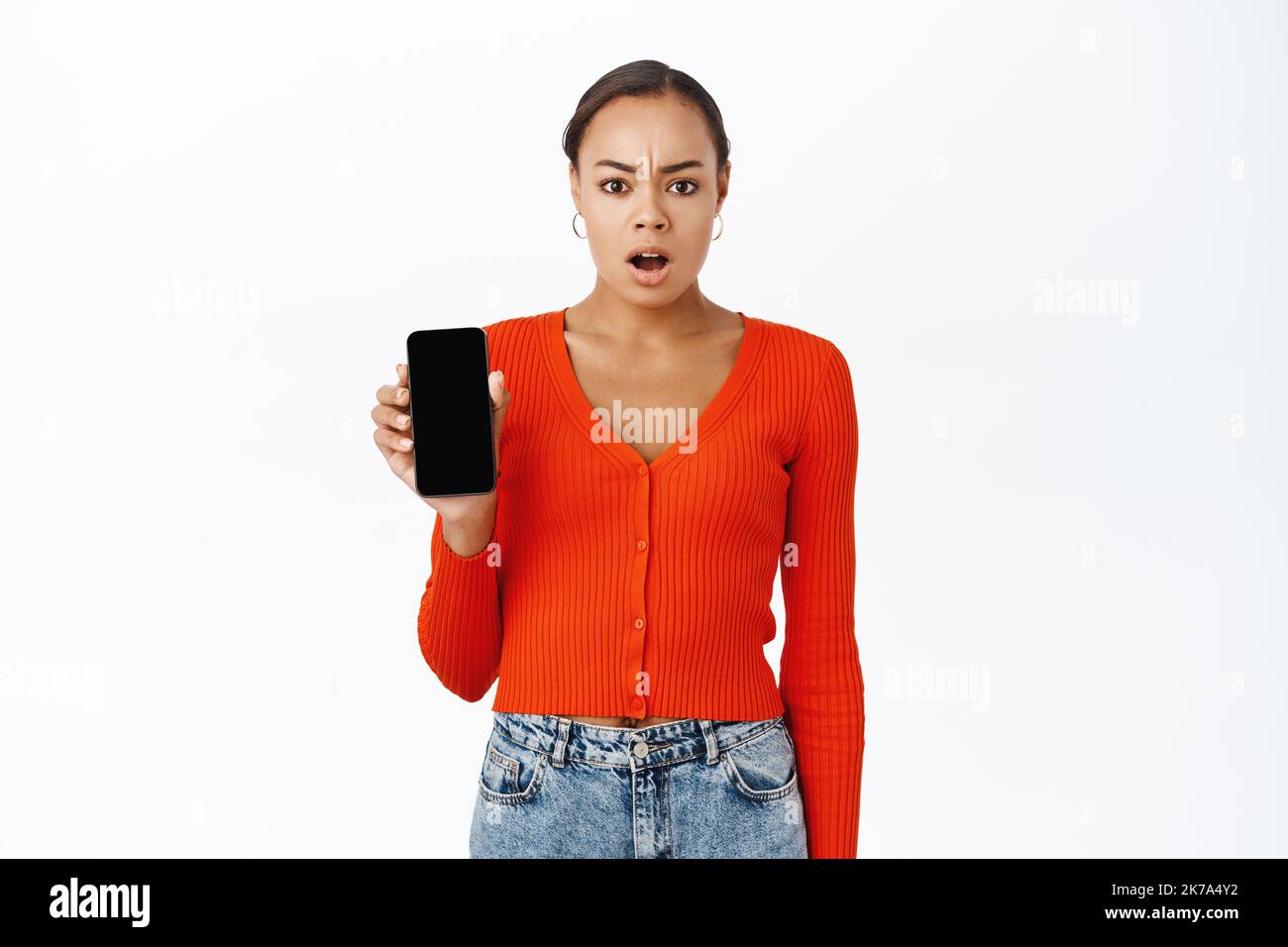 Shocked woman shows mobile phone screen, looks concerned at camera ...