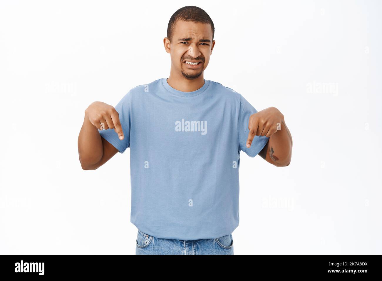 Disappointed man points fingers down with cringe grimace, dislike smth ...