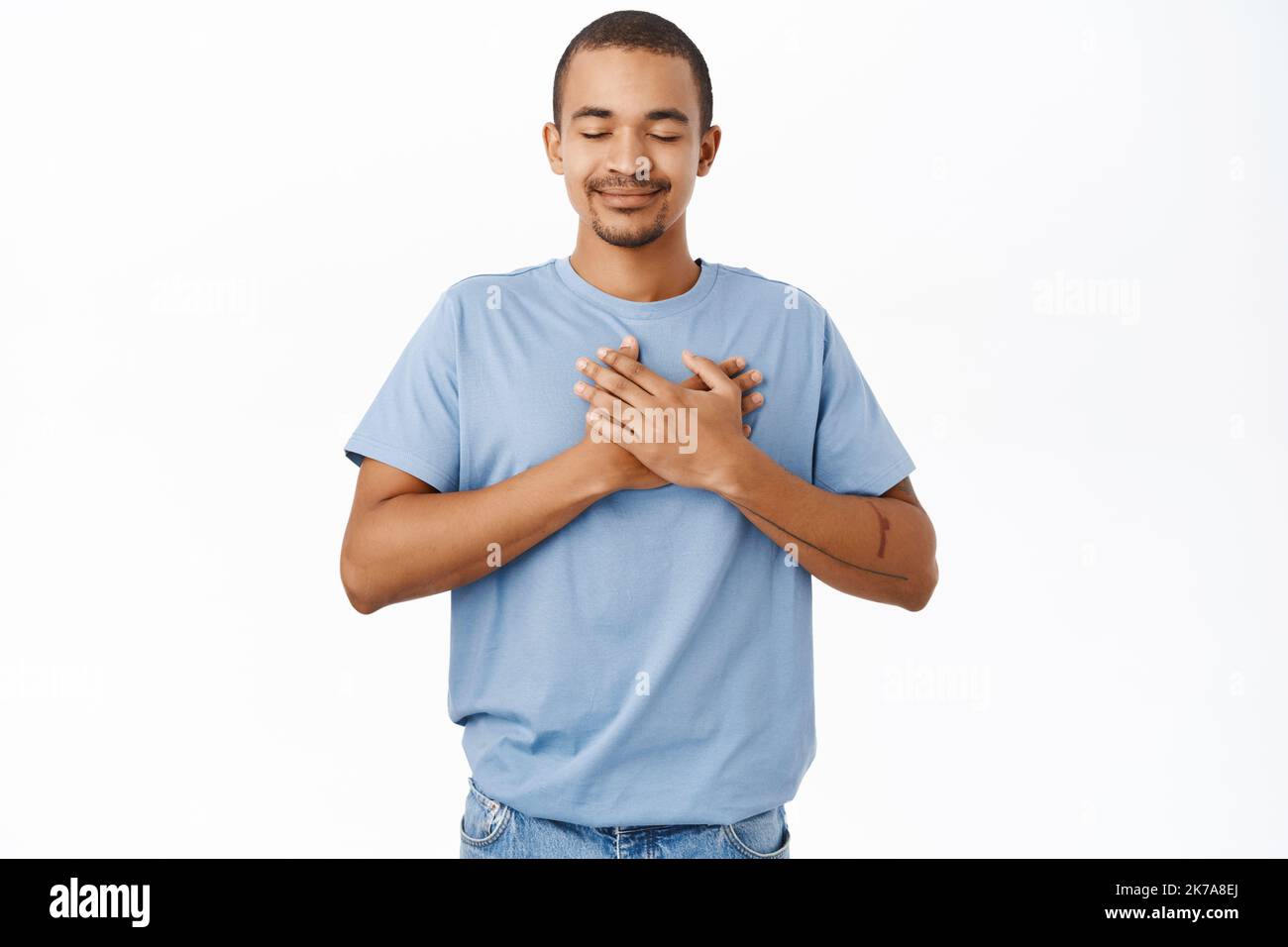 Smiling nice guy holds hands on heart, heartwarming and caring feeling ...