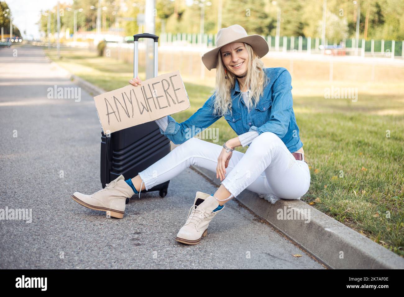 Happy woman wait passing car sitting with suitcase and cardboard poster ...