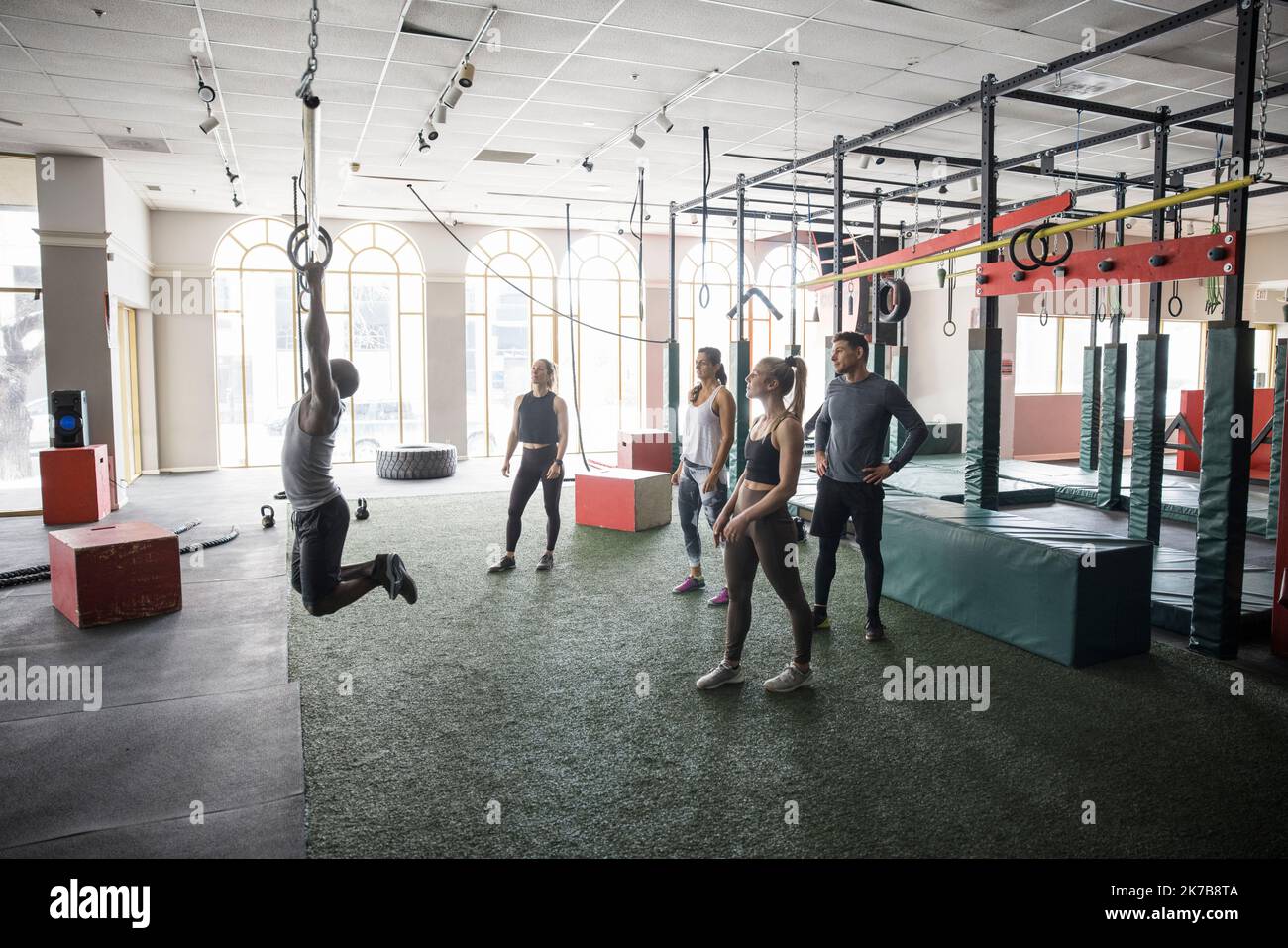 Cross training class watching instructor demonstrate pull ups on rings ...