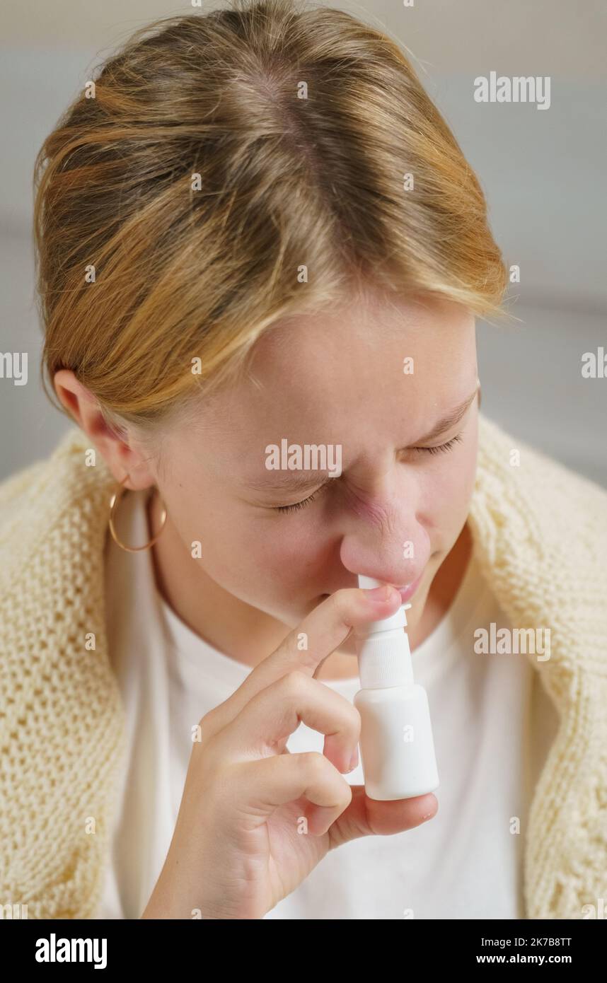 A girl with a cold treats a runny nose with a nasal spray. Vertical ...