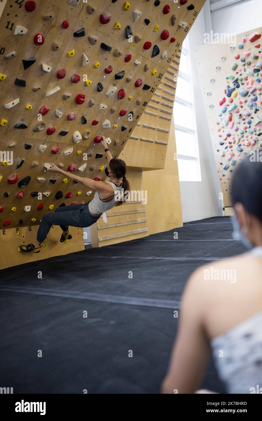 Female climber in face mask climbing session board in climbing gym ...