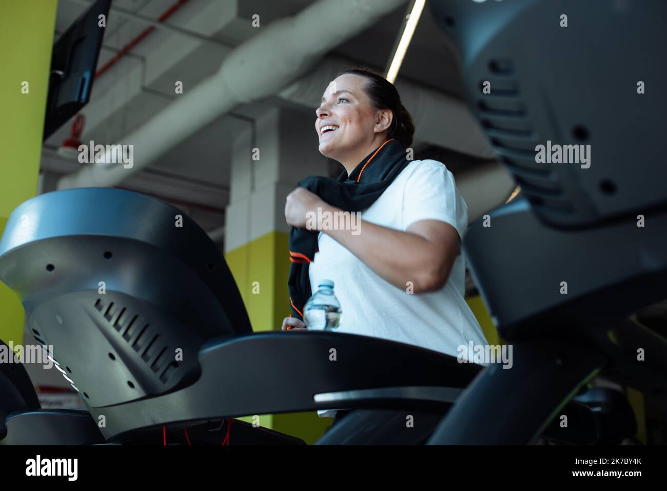 Smiling 40s years woman with pleasure run on treadmill at fitness gym ...