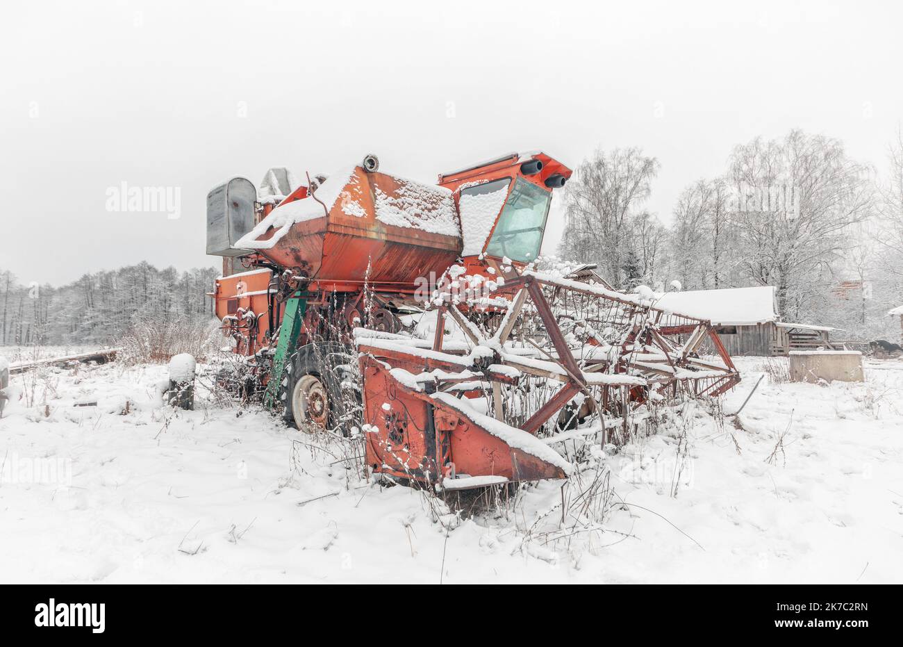 Red broken frozen combine harvester on a snow-covered field. Old broken ...