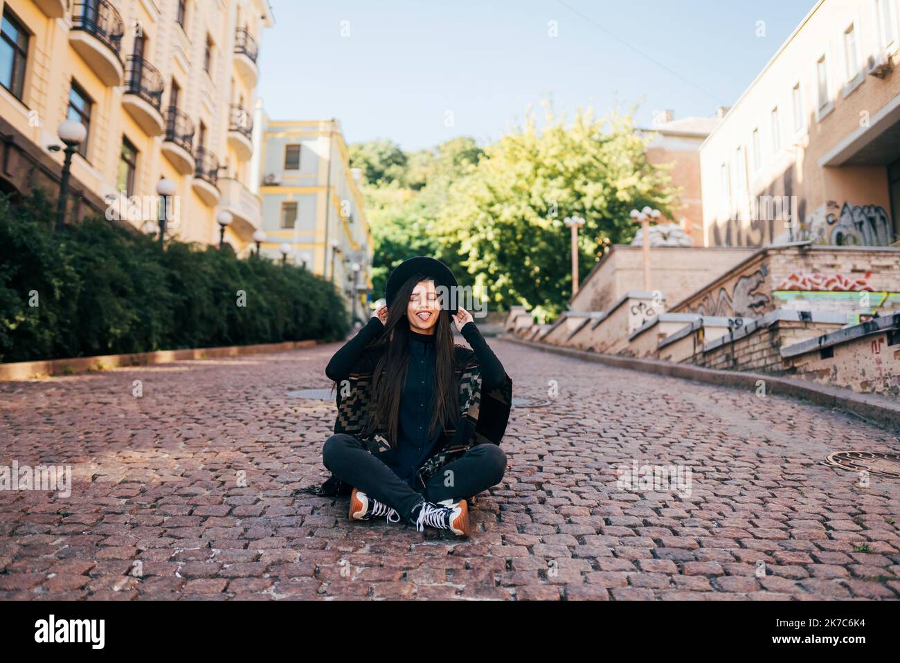 Young woman in hat sitting at city on cobblestone Stock Photo - Alamy