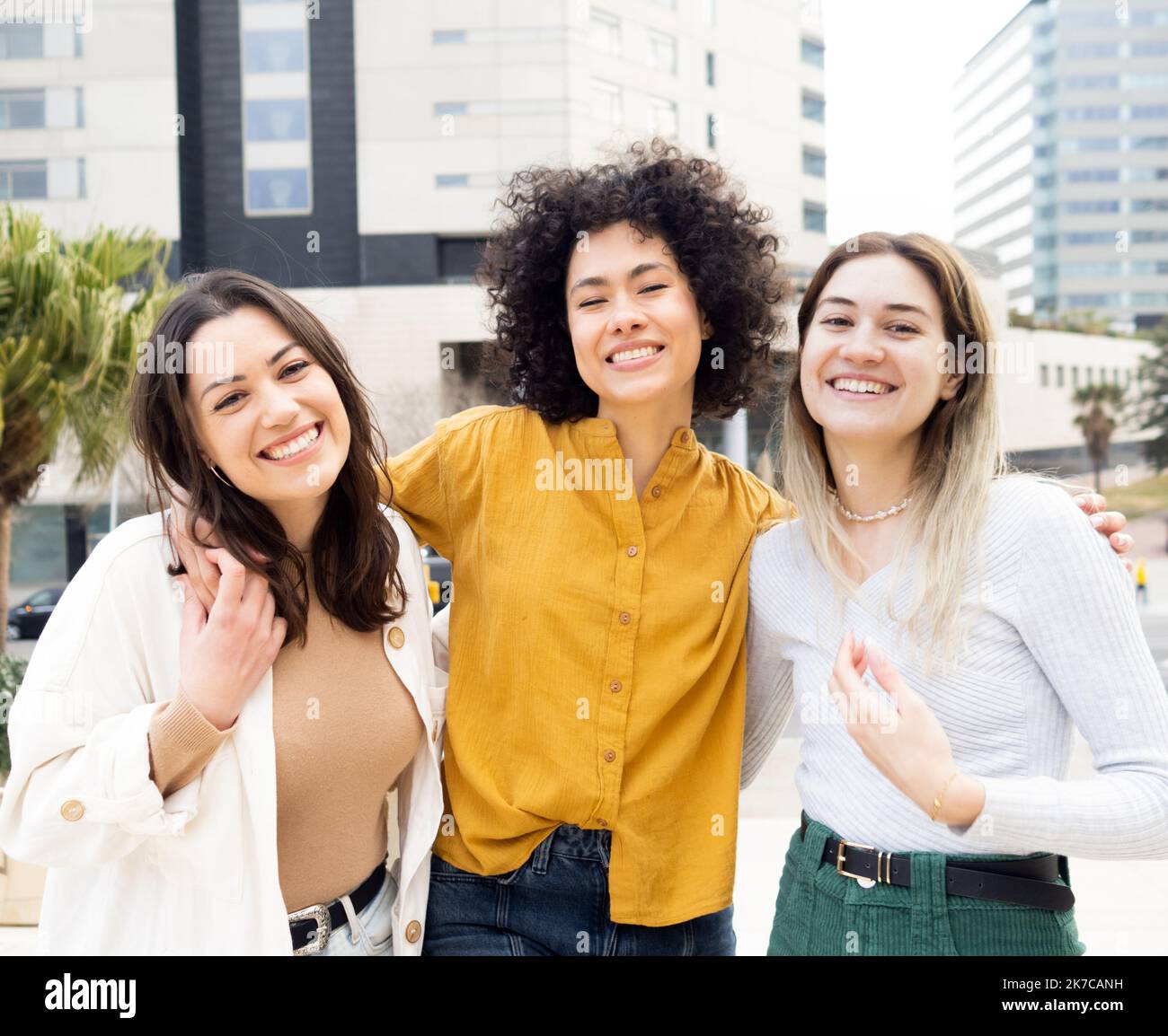 Three smiling diverse young women friends hugging looking at camera ...