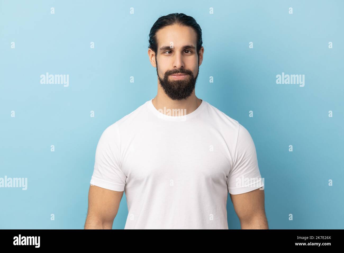 Portrait of comic positive man with beard wearing white T-shirt looking ...