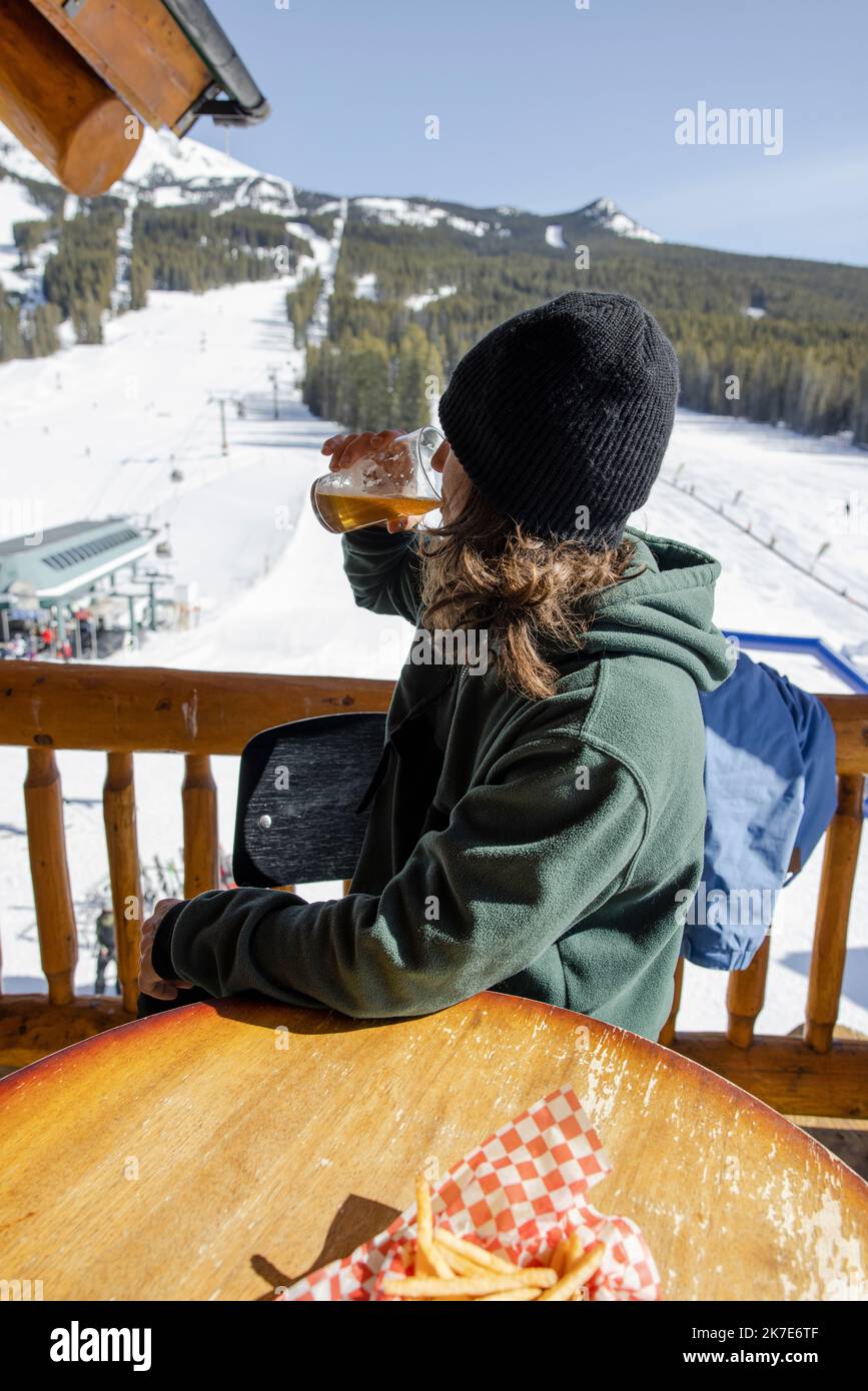 Man taking a break from snowboarding with beer on ski resort balcony ...