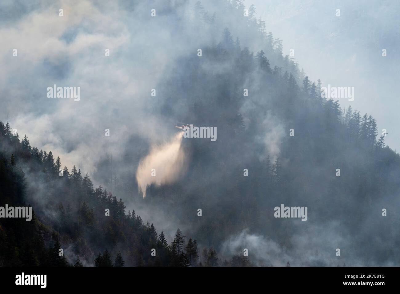 A helicopter drops water on a forest fire burning at the Nohomin Creek ...