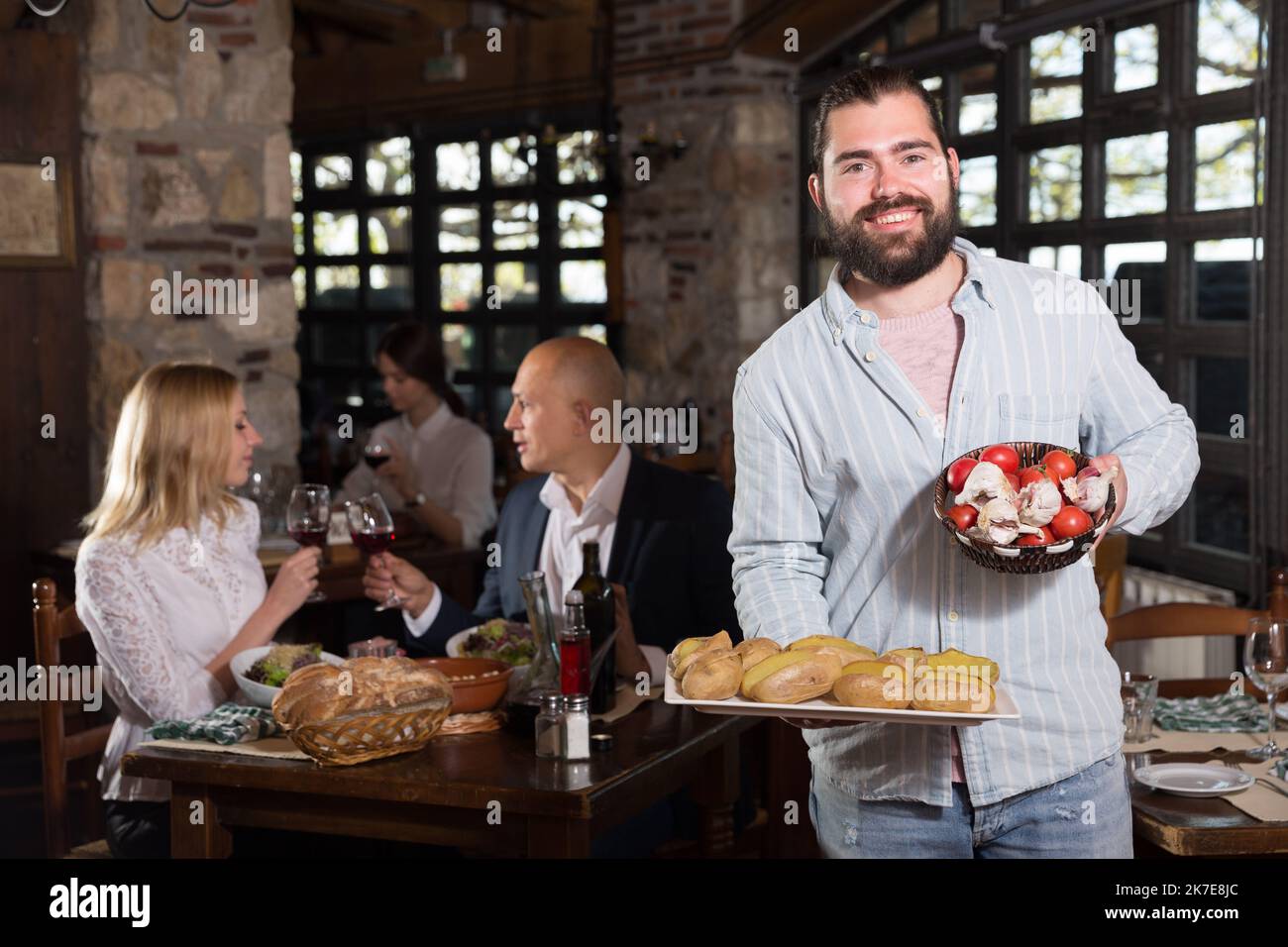 Positive male waiter welcoming guests to country restaurant Stock Photo ...