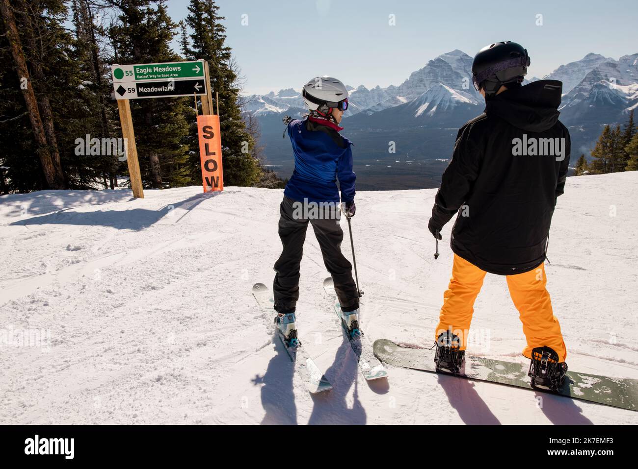 Skier and snowboarder talking at top of sunny scenic mountain slope ...
