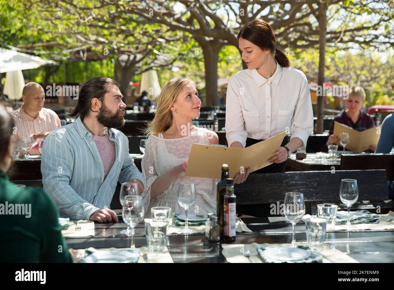 Waitress showing menu card to couple Stock Photo - Alamy