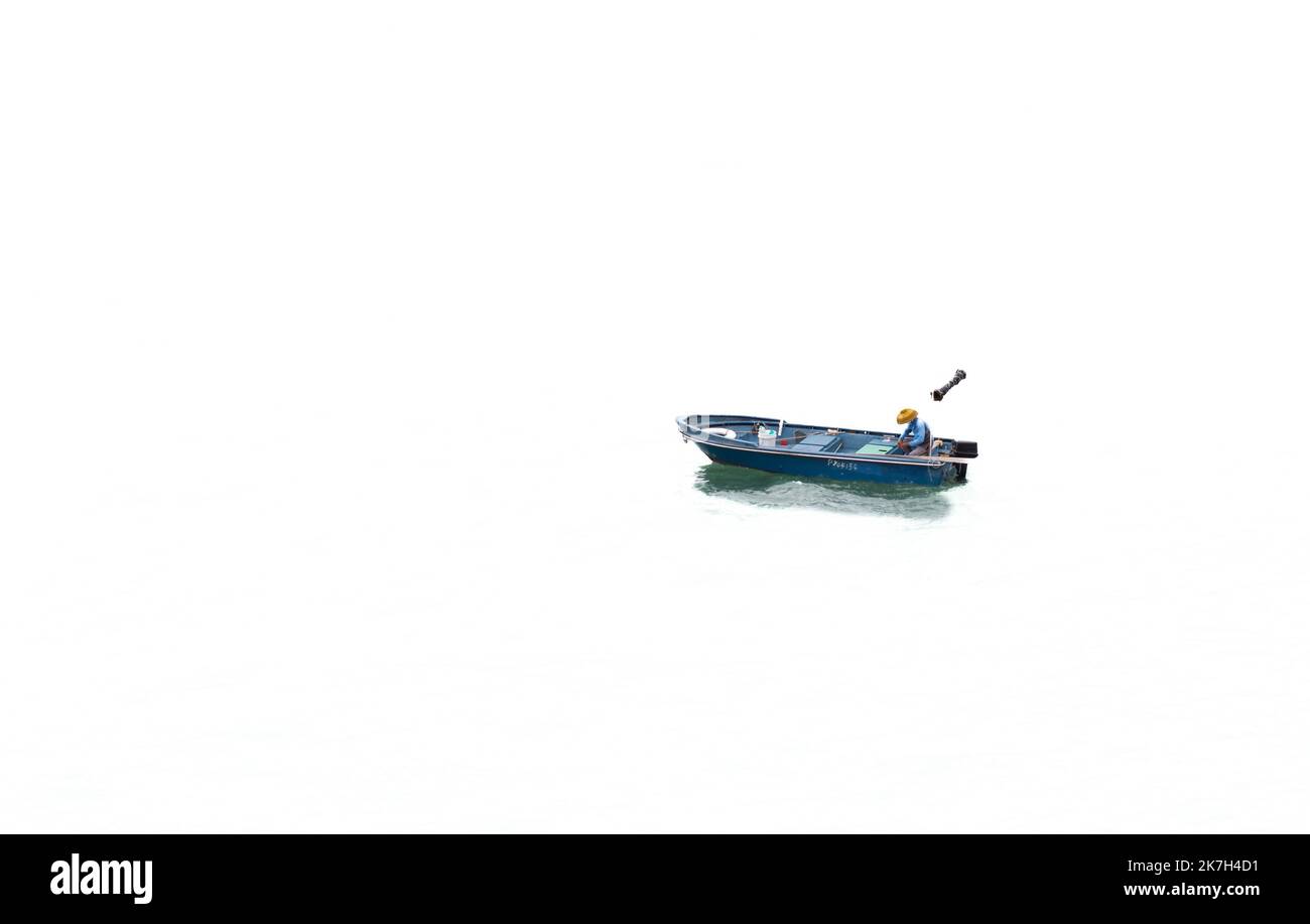 A fisherman works aboard a small boat. The sea is over exposed Stock ...