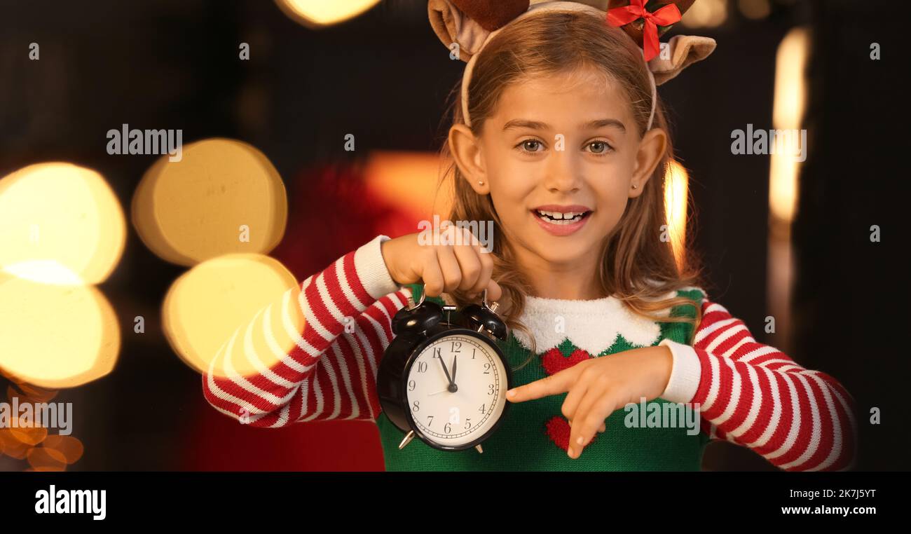 Cute little girl in elf costume holding alarm clock on dark background ...