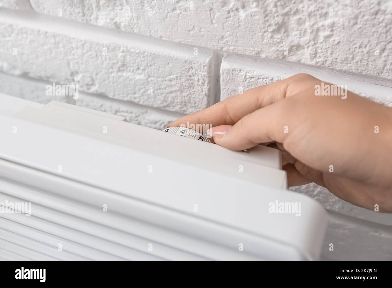 Woman adjusting radiator near white brick wall, closeup. Heating season ...