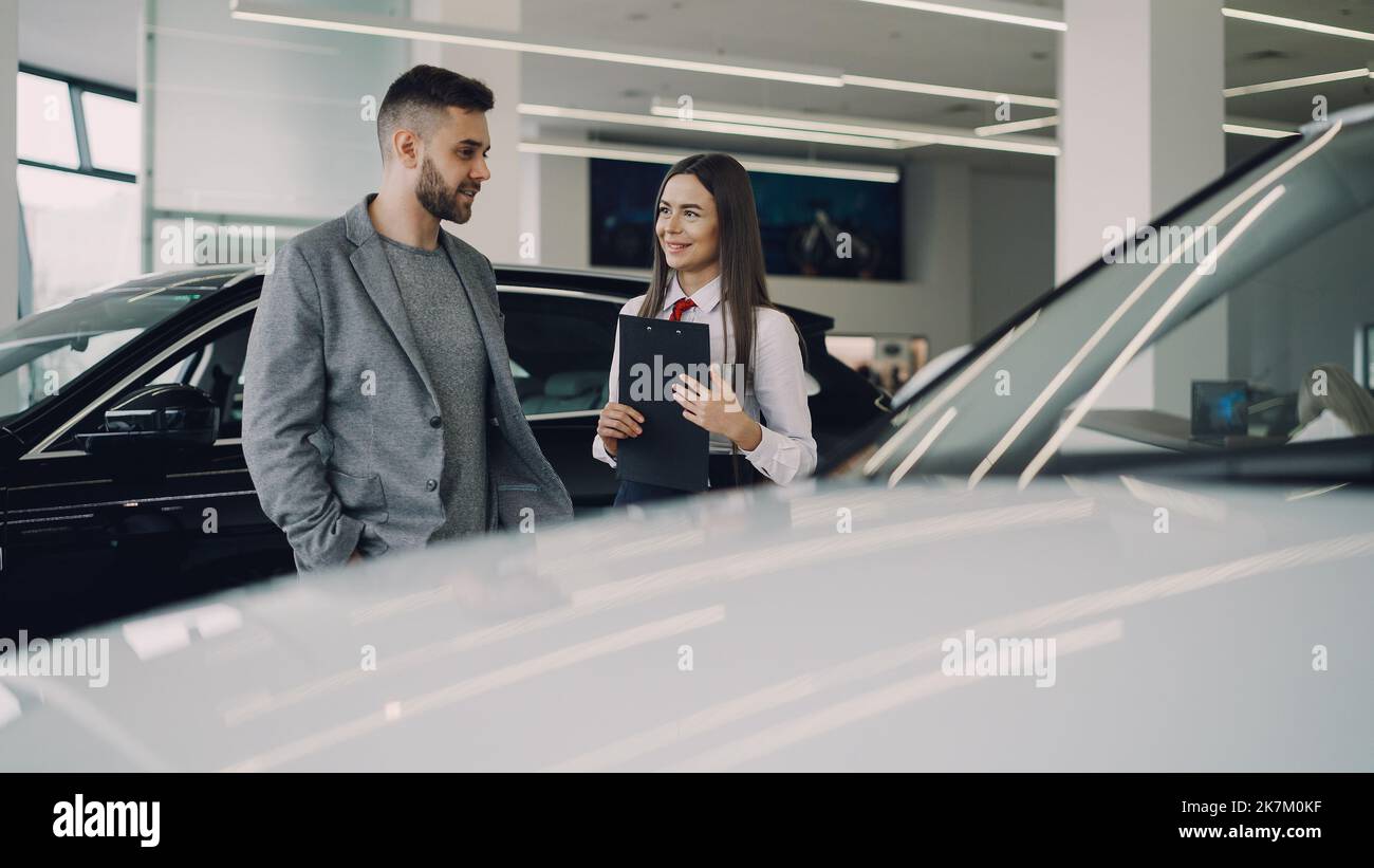 Attractive female car dealer is talking to interested customer about ...