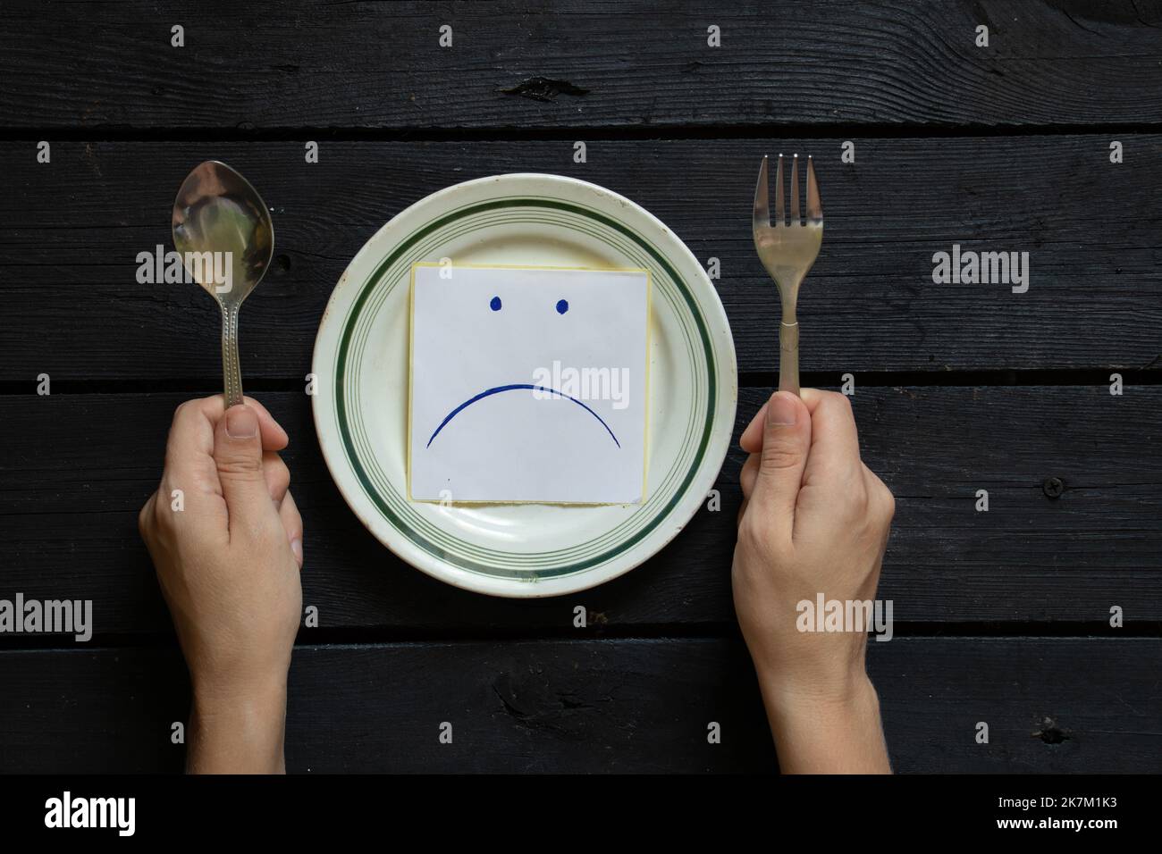 a plate of paper on which a sad smiley face and female hands are drawn ...