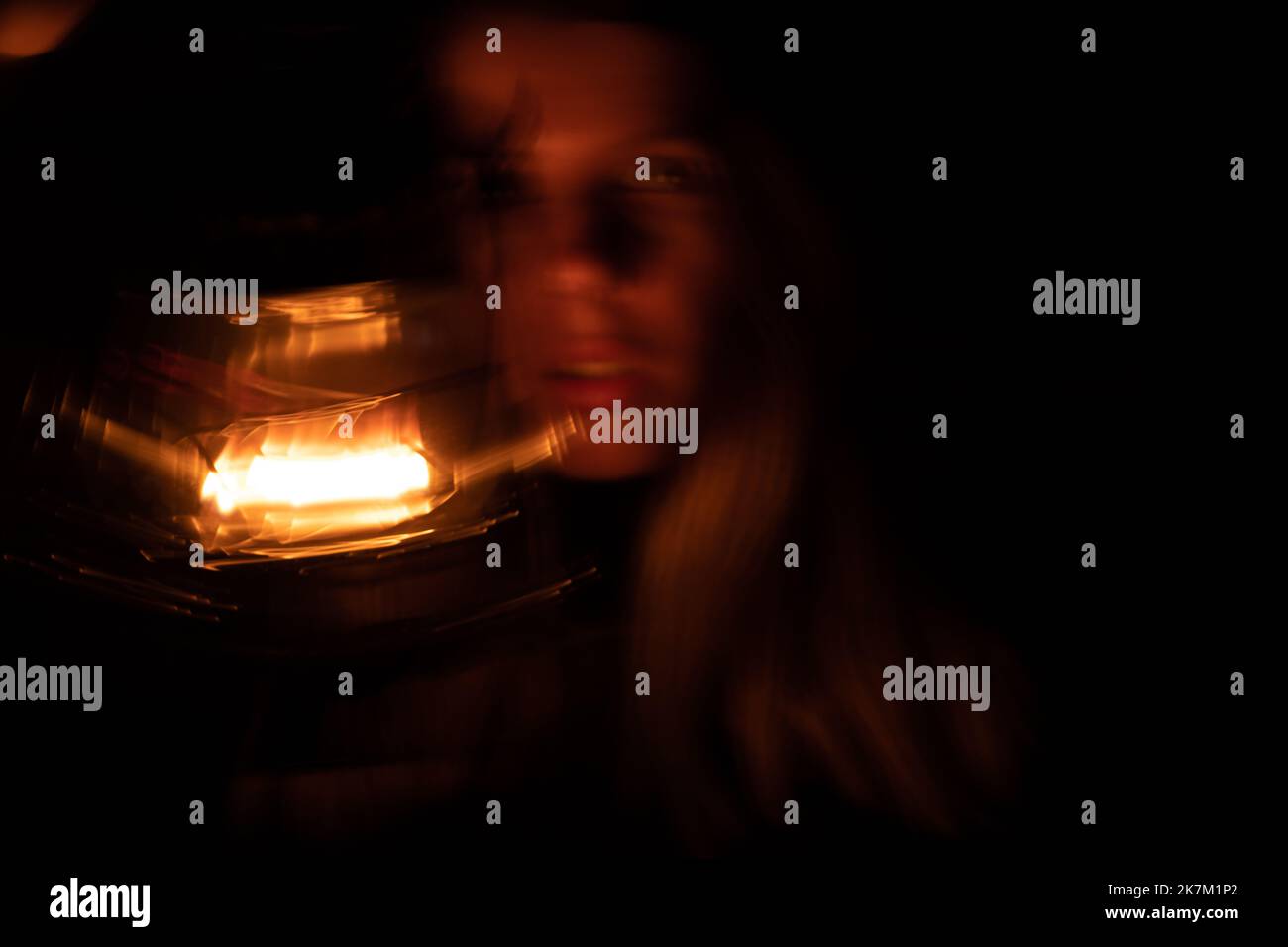 A young Ukrainian girl with a kerosene lamp in the dark sits at home ...