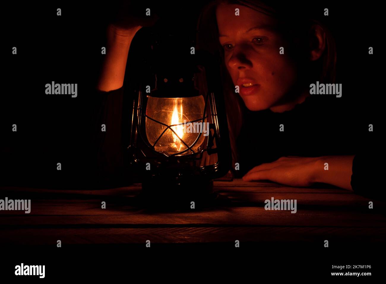 Young Ukrainian girl with a kerosene lamp in the dark sits at home ...