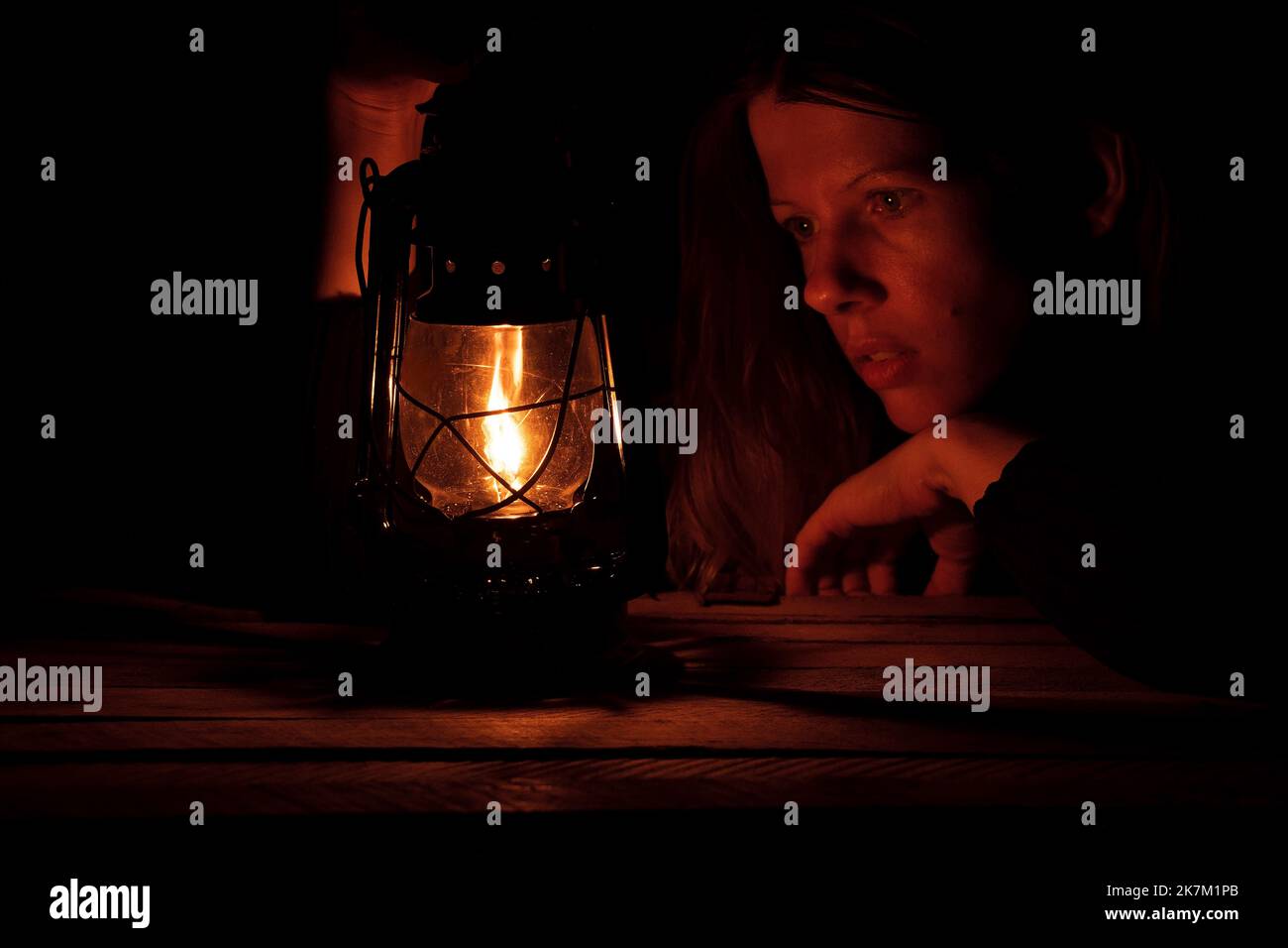 Young Ukrainian girl with a kerosene lamp in the dark sits at home ...
