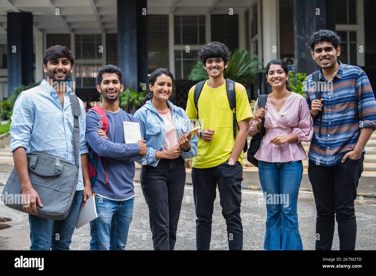 Group of happy students standing with books and backback by looking camera at college campus ...