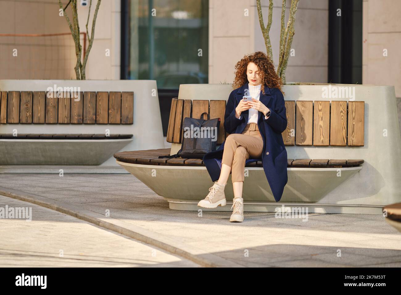 Serious woman sitting on bench and checking message on her smartphone ...