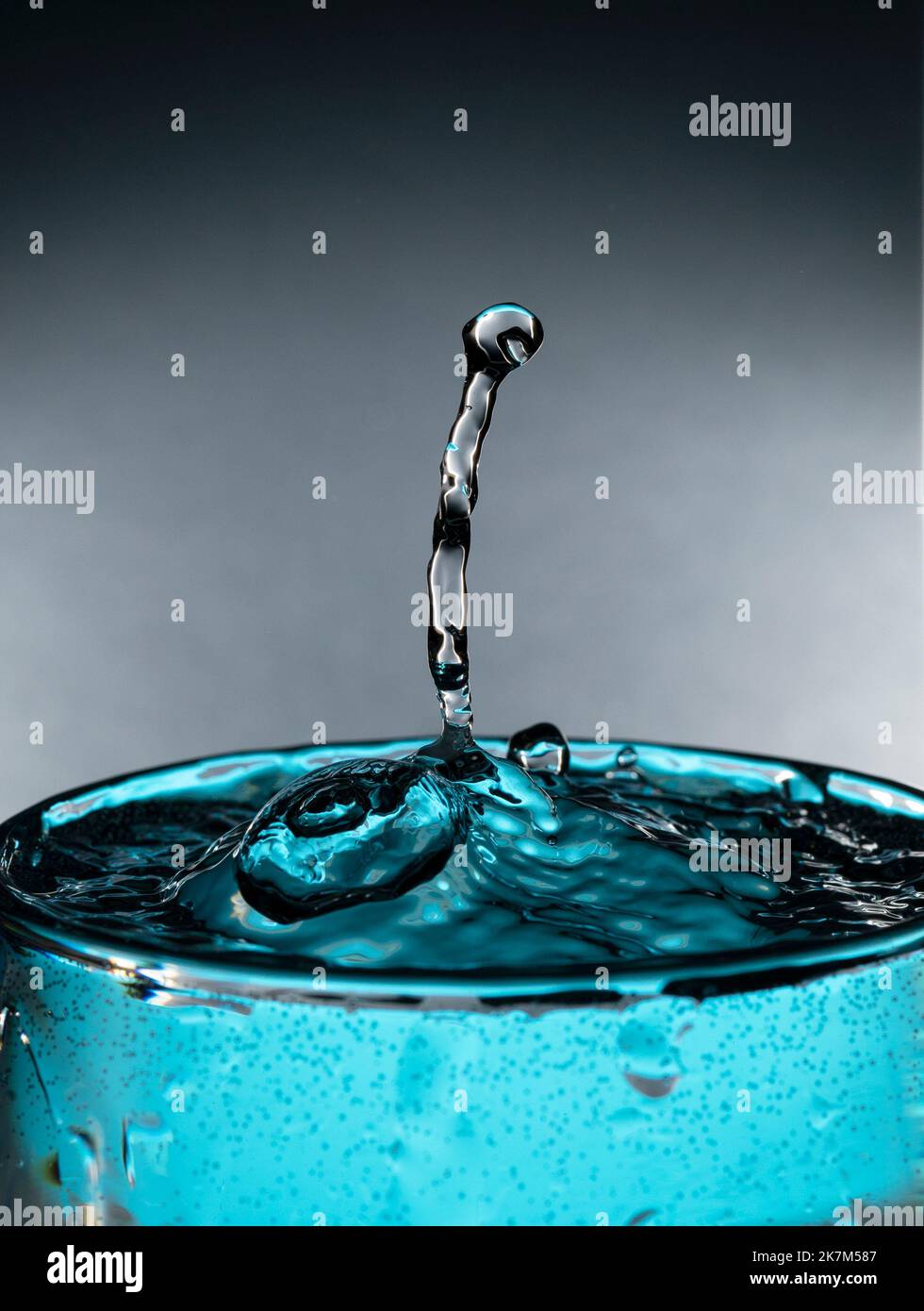 Water drop splash in a glass cup blue colored Stock Photo - Alamy