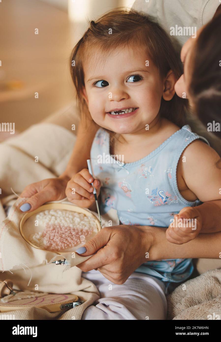 Woman with her little daughter sitting on the floor embroidering with a ...