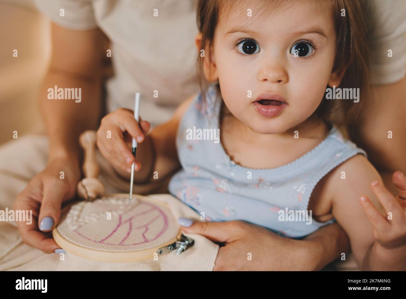 Mother learning baby girl how to embroider a pattern on the white ...