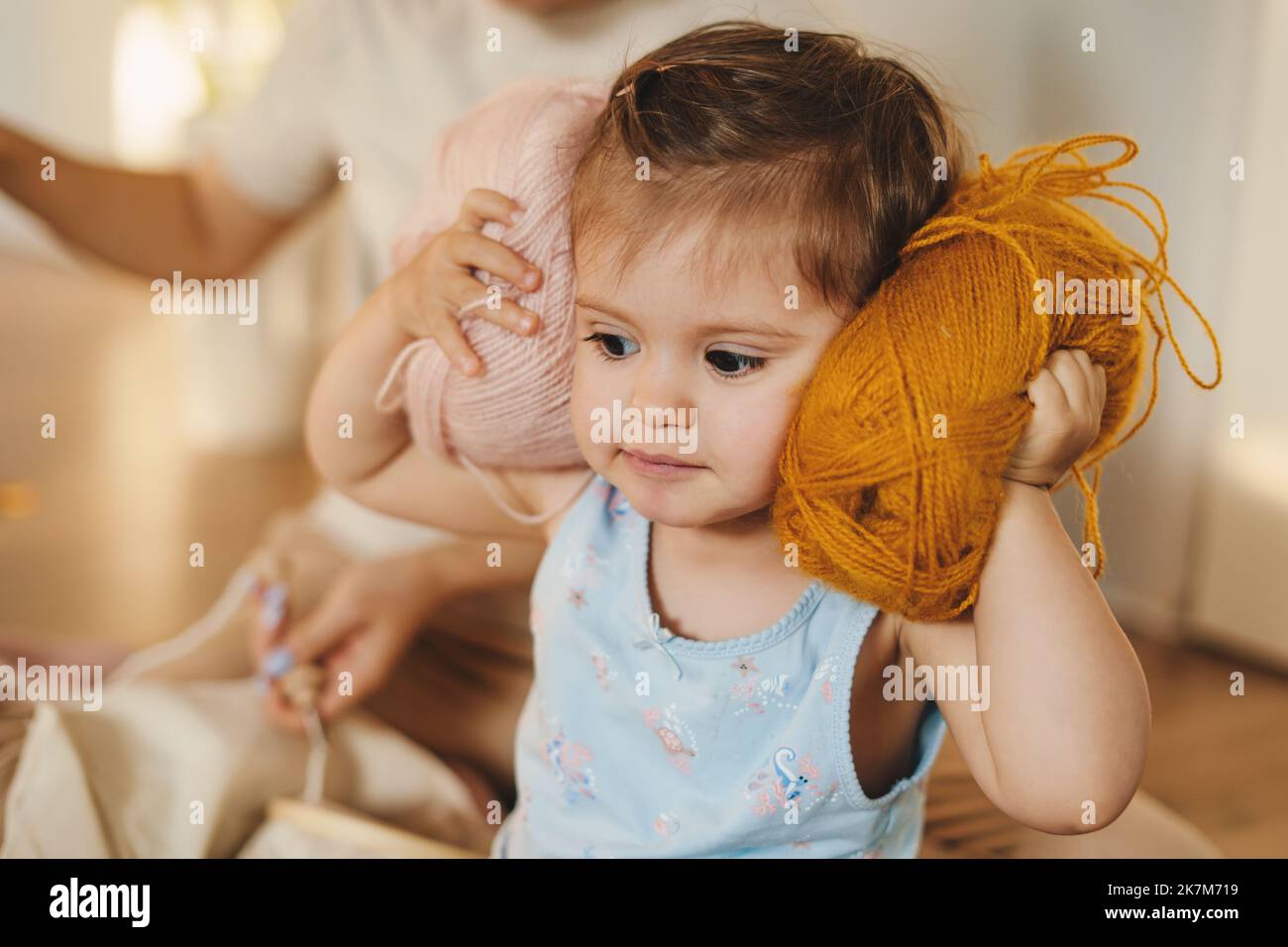 Funny portrait of a baby girl holding two large balls of thread to her ...